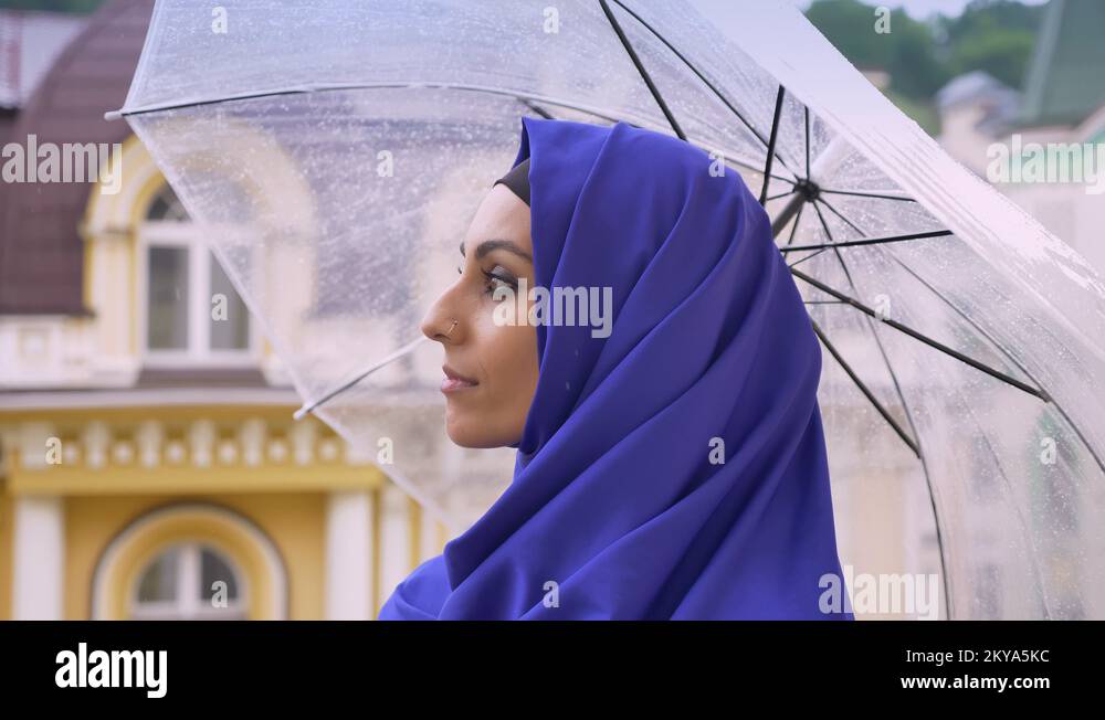 Profile of young muslim woman in hijab holding umbrella during rain ...