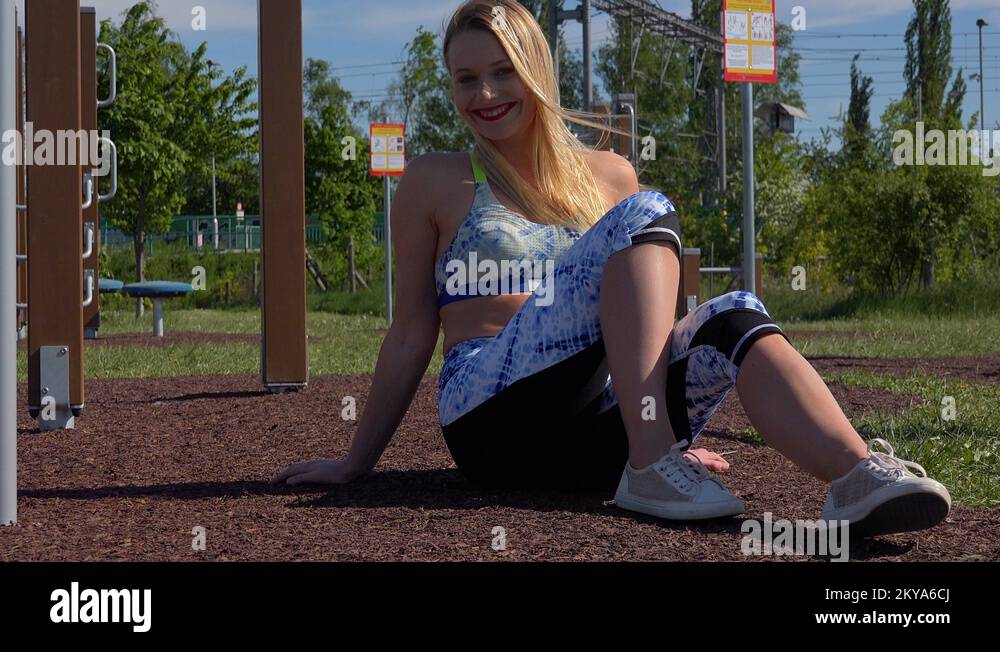 A fit beautiful woman smiles at the camera and sits on the ground at an ...