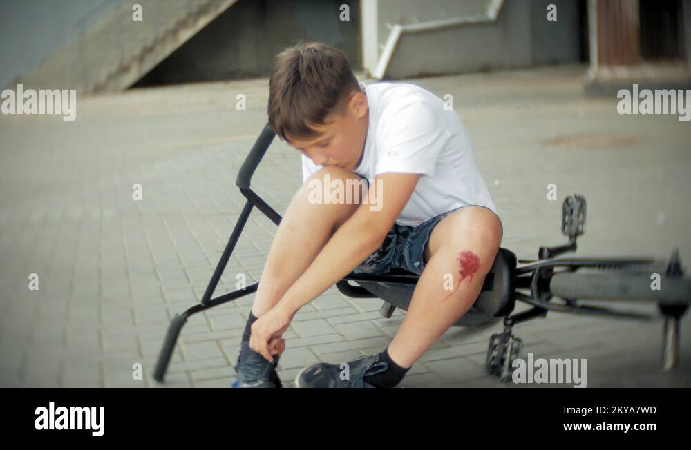 A young boy sits in a park after falling from a bike, calms the pain in ...