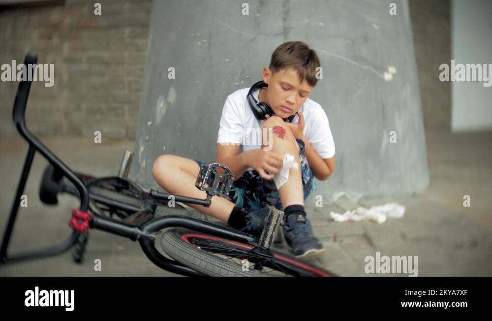A young boy sits in a park after falling from a bike, calms the pain in ...