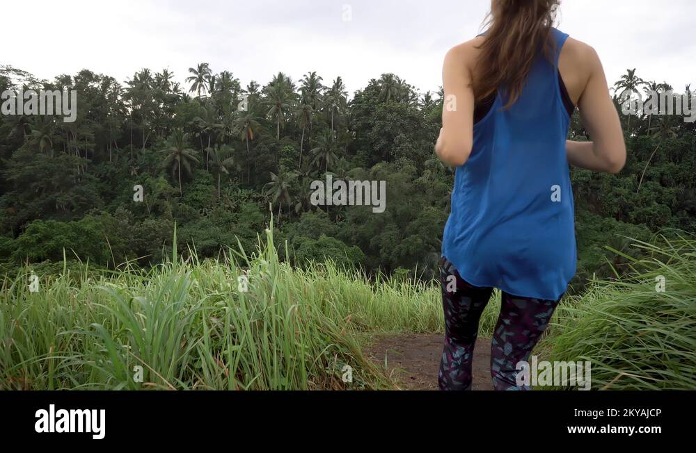 Woman runner in sports wear raise arms up in the air looking on jungle ...