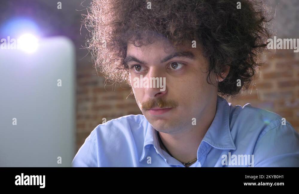 Funny nerd hacker typing on laptop and looking at camera smiling, brick ...