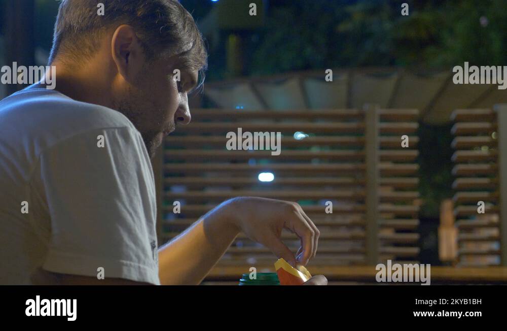 A sad person sitting in a fast food restaurant outside at night eats ...