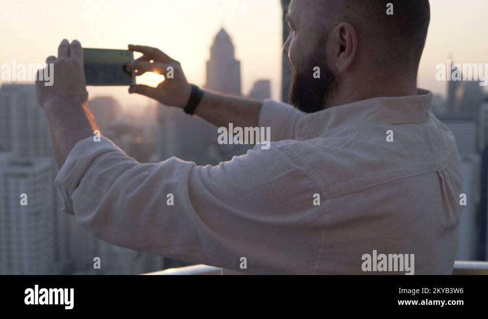 Man standing on the rooftop and doing photos of the city during sunset ...