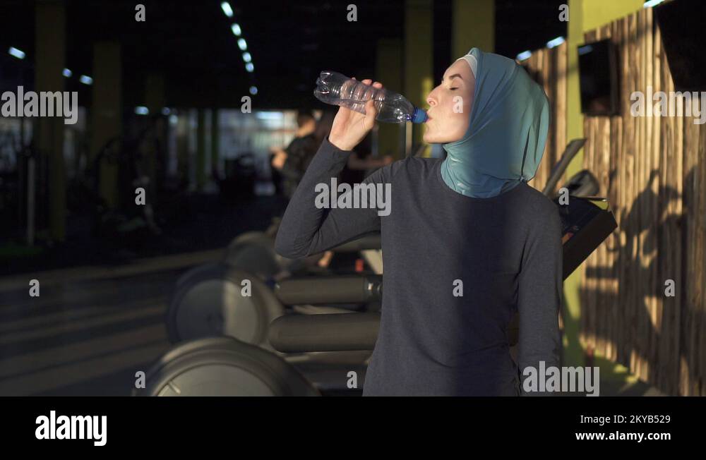 Young sporty muslim girl in hijab drinking water from bottle after ...