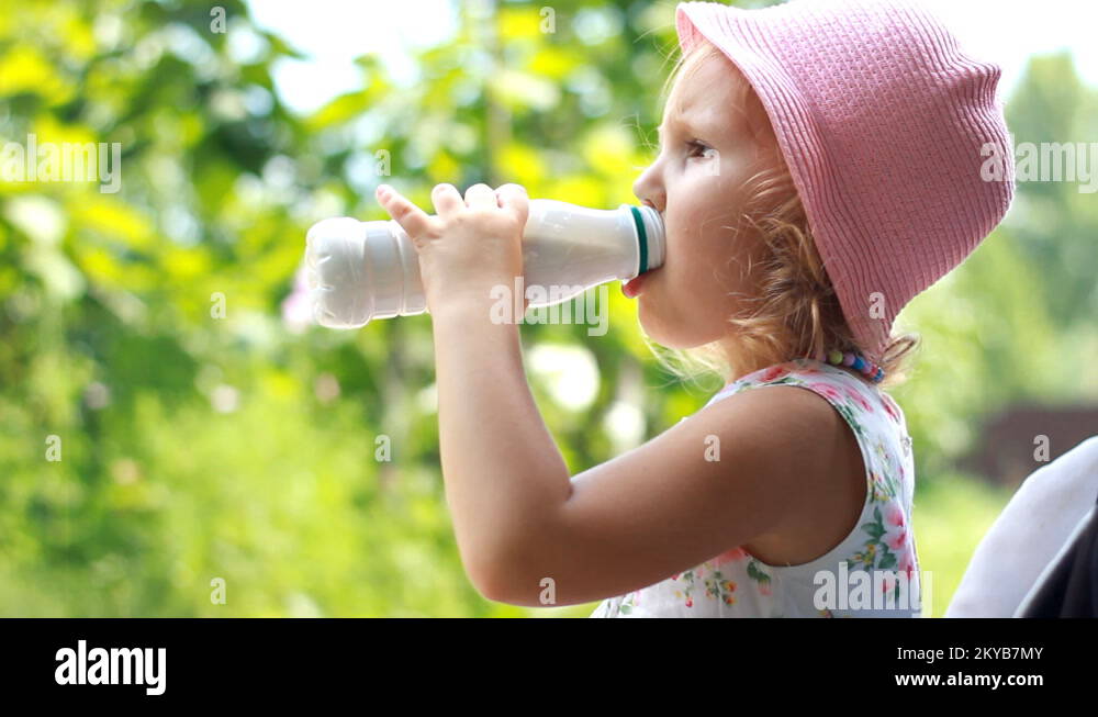 Child girl drinks a milk drink from a bottle or kefir, smiles and shows ...