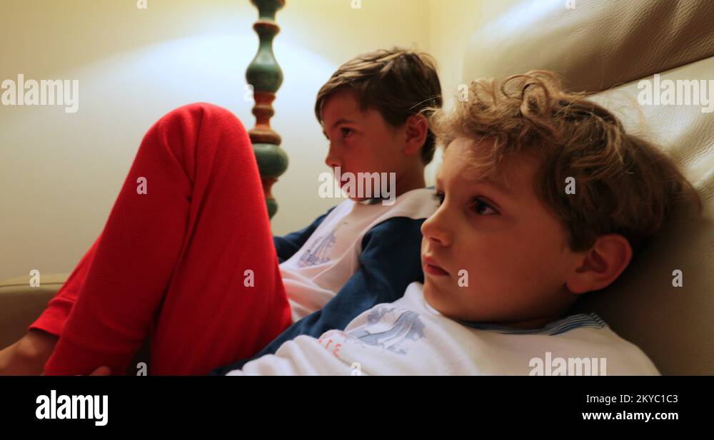 Boys seated on sofa watching TV off camera. 4K candid clip of children ...