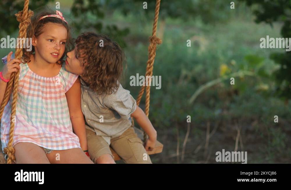 Loving boy and girl ride on a swing sitting next to each other. The boy kisses Stock Video ...