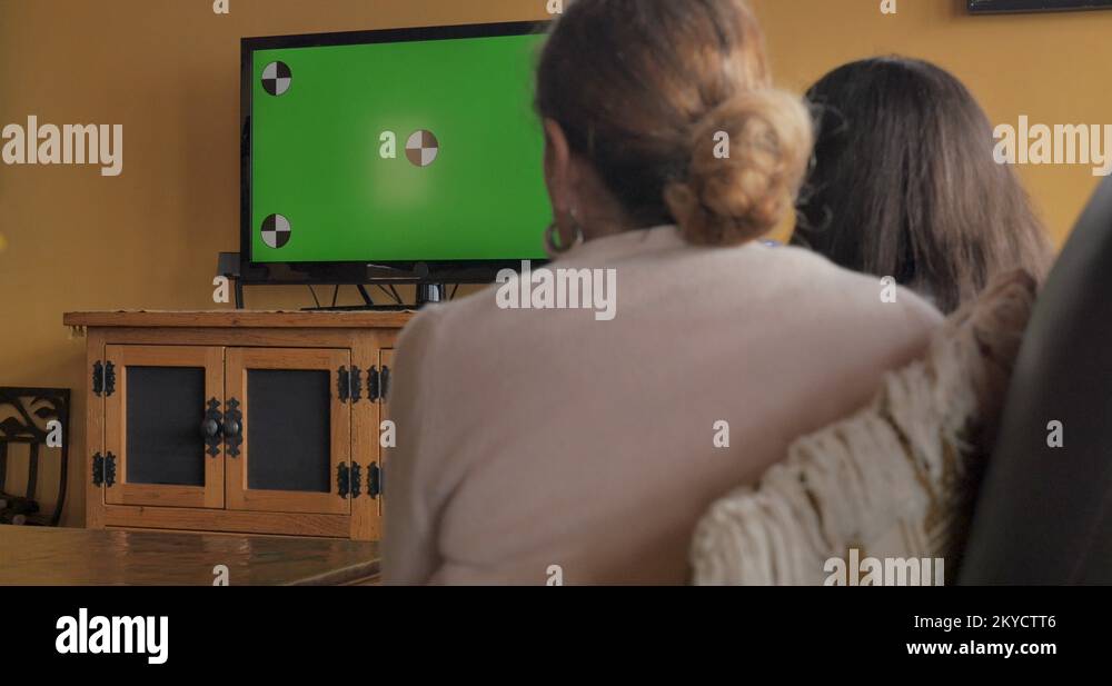 Female parent and daughter watching a green screen television together ...