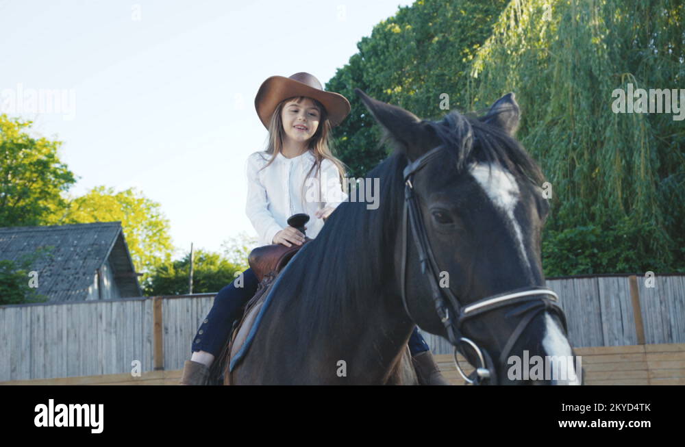 Pretty little girl in hat riding a black mare on the arena. 4K Stock ...
