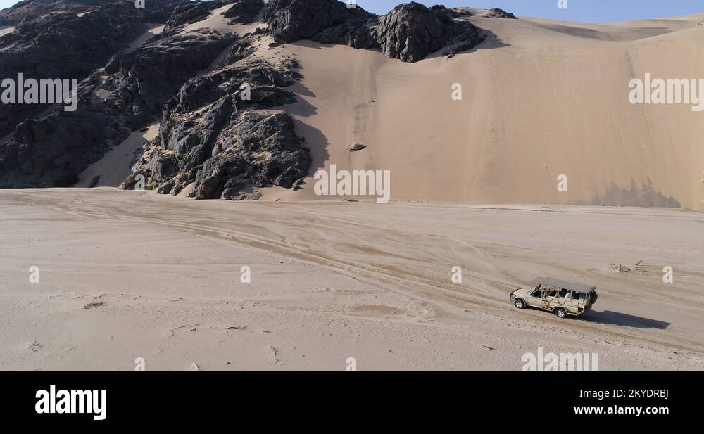4K aerial zoom out view of a safari vehicle driving next to sand dunes ...