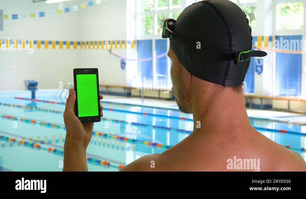 A swimmer looks at a smartphone with a green screen at an indoor pool ...