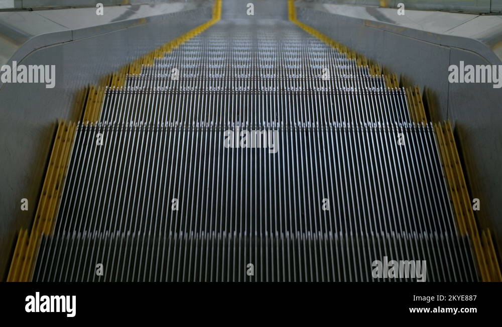 A close-up of the steps of the escalator rising up. The guy's feet are ...