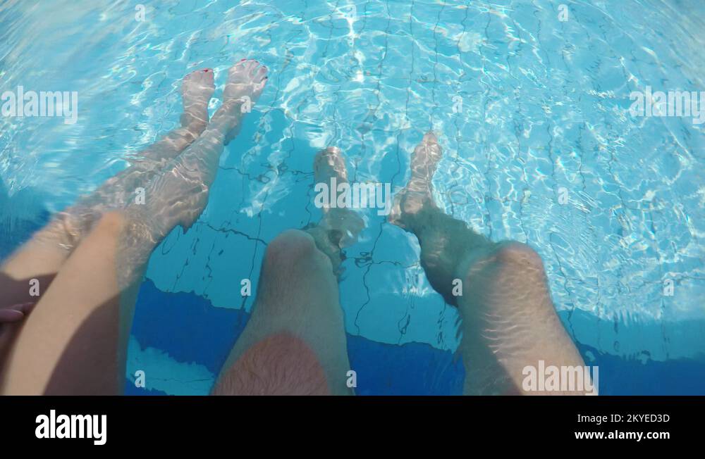 Man and woman sitting on pool edge, splashing water with their feet on ...