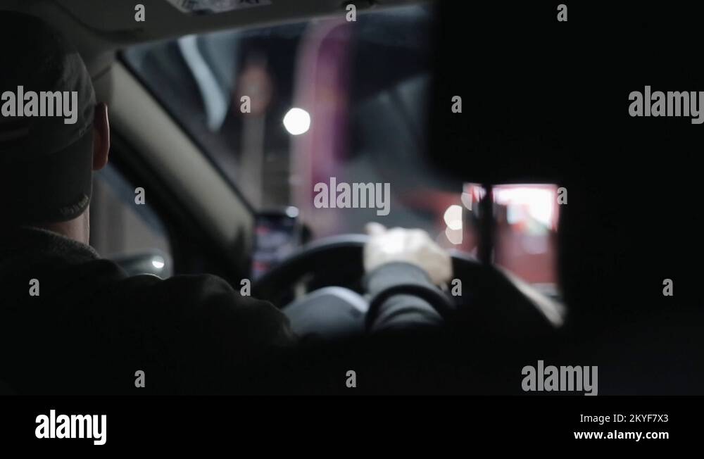 A smiling male driver wearing a cap backwards makes a turn. Driving at ...