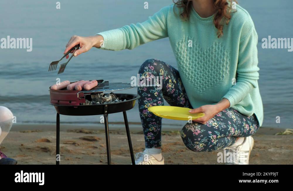 Mother and daughter fry meat and vegetables on a barbecue on the beach ...