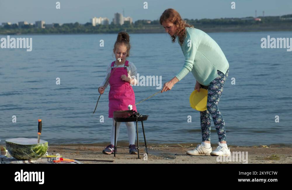 Mother and daughter fry marshmallows and vegetables on a barbecue on ...