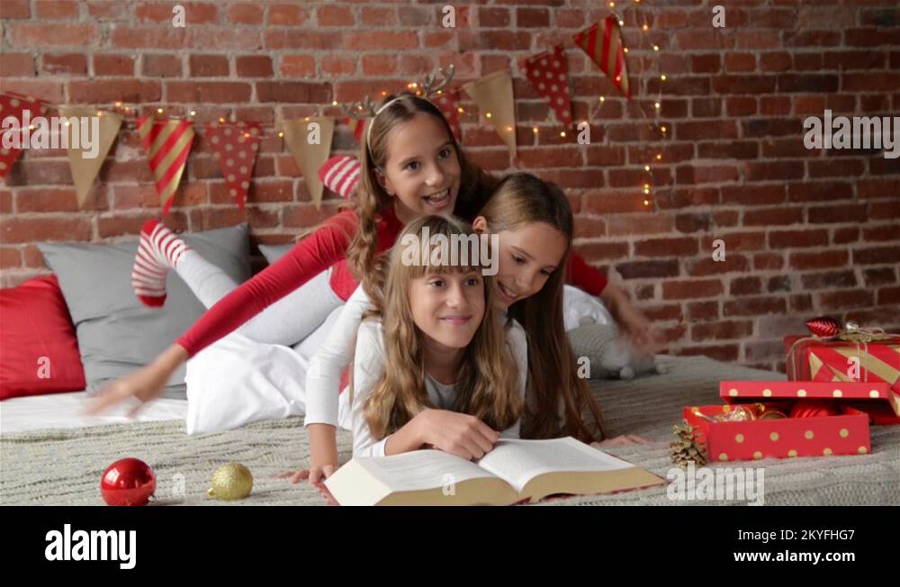 Triplets sisters dressed in xmas pajamas are playing on the bed, which ...