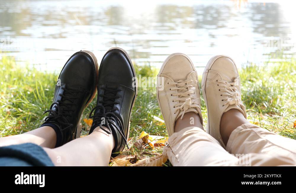 2 Two pares of female legs in footwear lying on a park grass near water ...