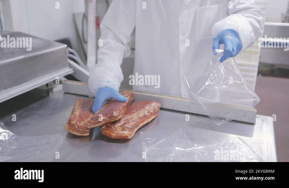 Meat processing worker packs smoked meat in vacuum packaging Stock ...