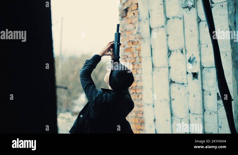 Boy in black clothes holding gun and looking up. Teen waiting for ...