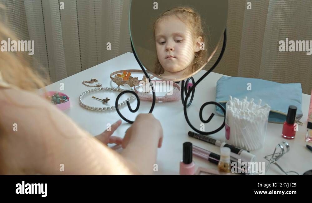 little girl with red hair smears cream, looks in the mirror, makeup ...