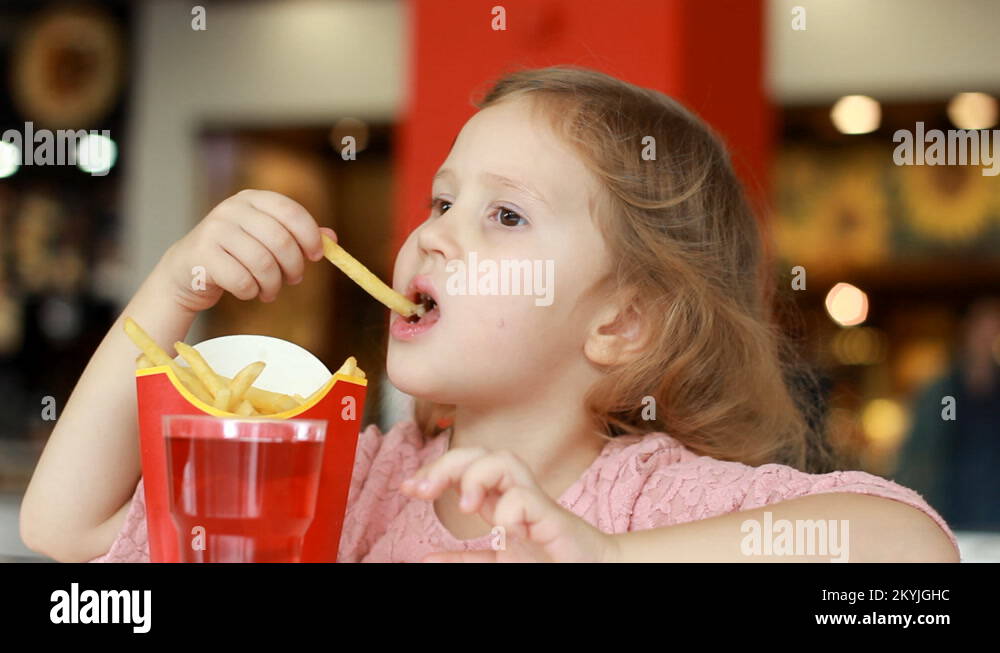 Child girl eating fast food french fries and drinking juice in a cafe ...