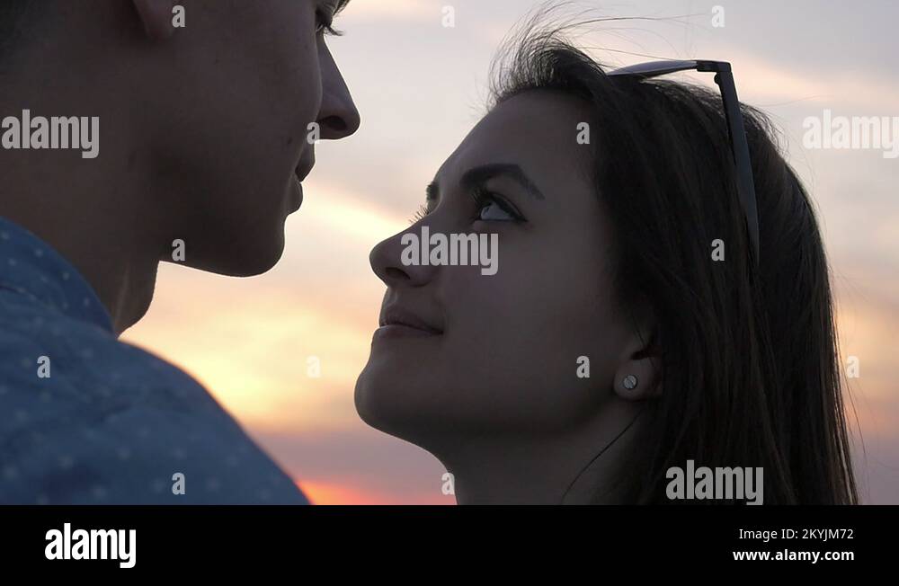 Cutie girl kissing her happy boyfriend touching his nose at sunset in ...