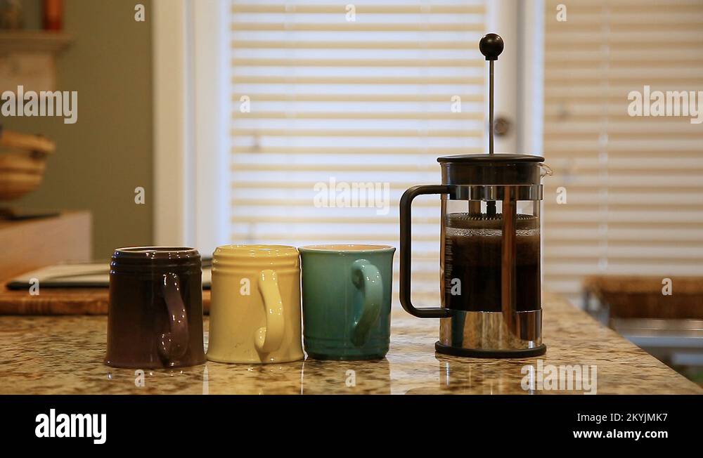 A french press on a kitchen counter top being pressed followed by ...