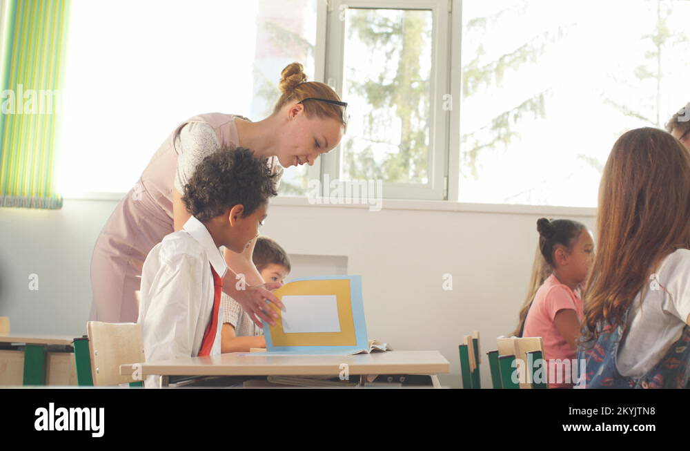 Teacher helping kids with their homework in classroom at school Stock ...