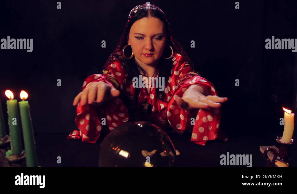 A gypsy fortune teller at the table reads the future in a magic ball ...