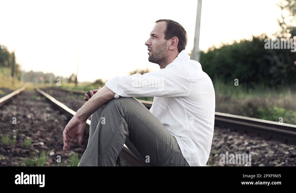Sad, angry man sitting on railroad track HD Stock Video Footage - Alamy