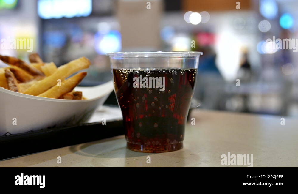 A cup of coca cola and fries on table at food court inside shopping ...