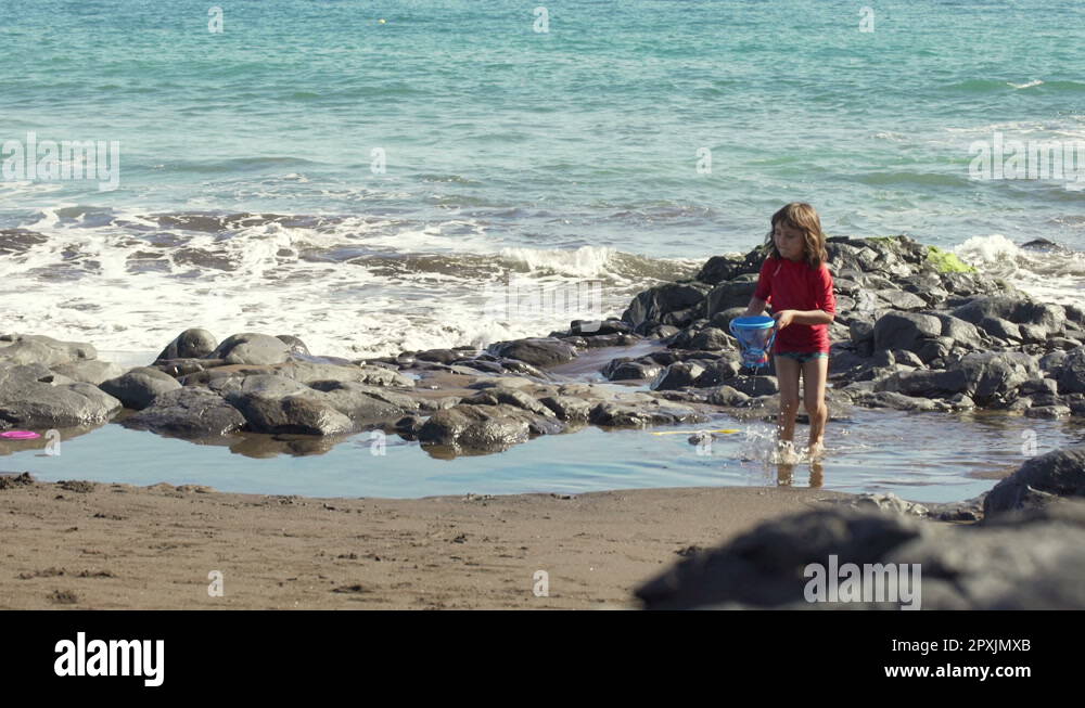 Boy walking on the beach with a bucket and pouring water, steadycam ...
