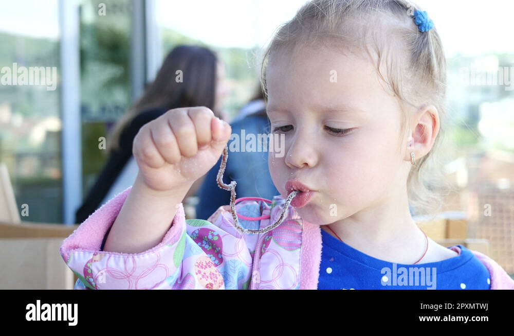 Little girl eating a long sweet sugar candy pasta tightening in mouth ...