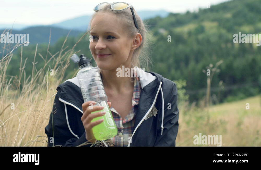 Pretty girl standing on the hill in the meadow and drinking energy ...