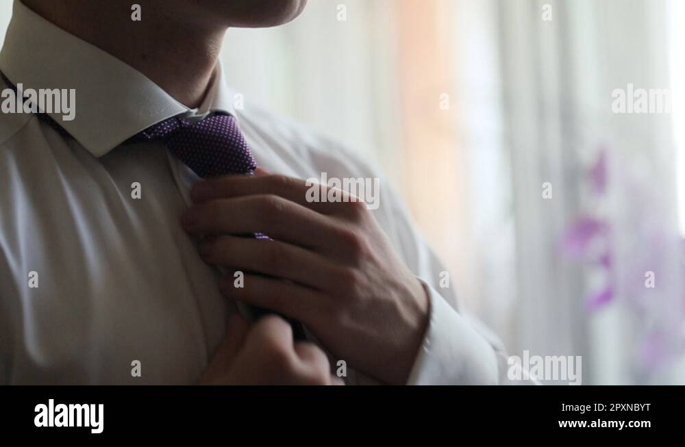 A picture of a groom fixing a fine tie carefully, neat white shirt on ...