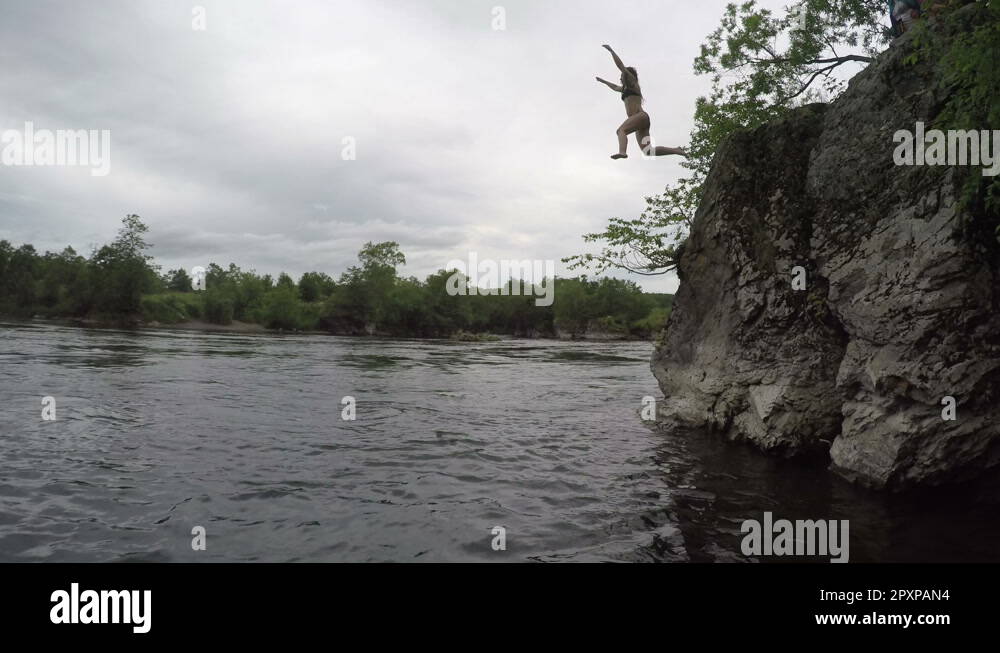 Fearless cute young woman jumping from high cliff into cold water of ...