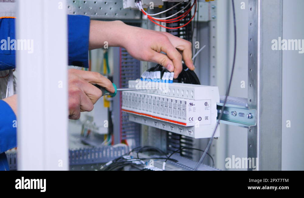 Unrecognised man fastens the connections in fuse box, electric rack ...