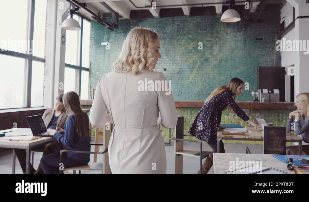 Beautiful blonde female team leader walk through the office, controls ...