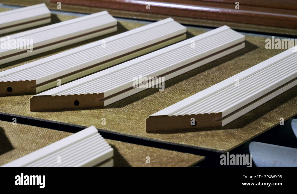 Wooden parts covered with varnish are being unloaded on a conveyor belt ...