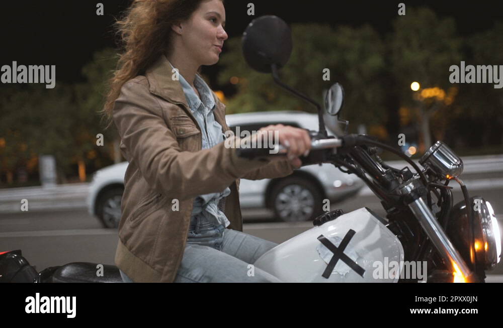 Beautiful young woman riding an old cafe racer motorcycle on street ...