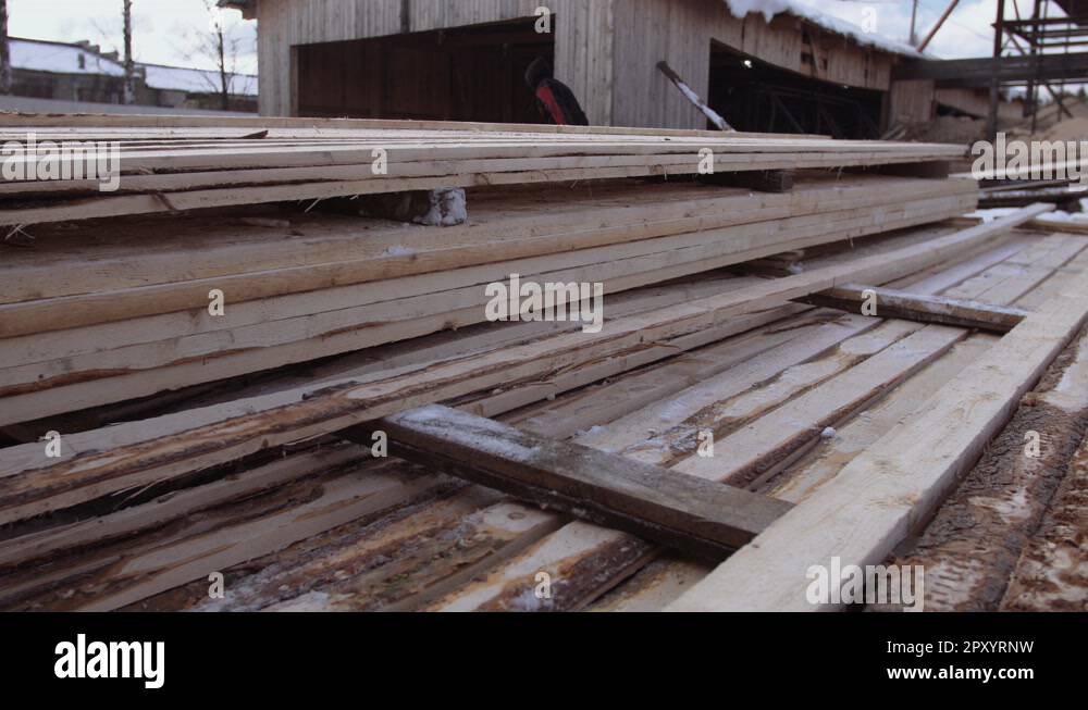 Man working at stacks of packed lumber planks stored in yard of sawmill ...