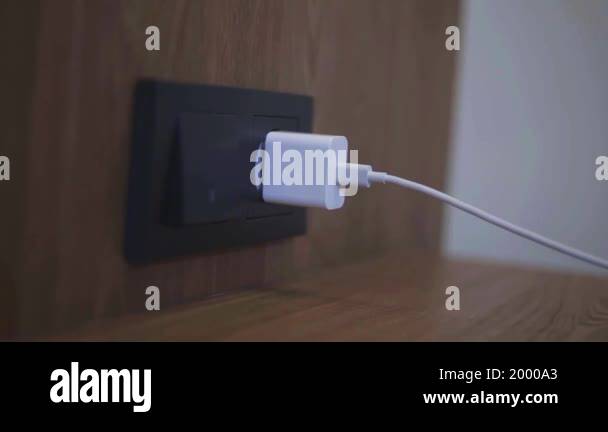 Hand unplugging mobile charger from electric socket. Unknown guy ...