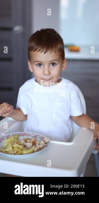Cute child sits at high chair pointing at his plate. Little baby having ...