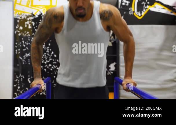 Strong african athlete doing push ups on parallel bars at sport club. Muscular afro american ...
