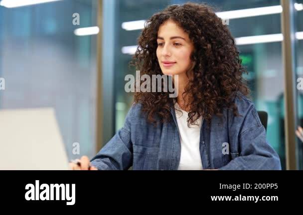 Confident female employee with long curly hair smiles at the camera in ...