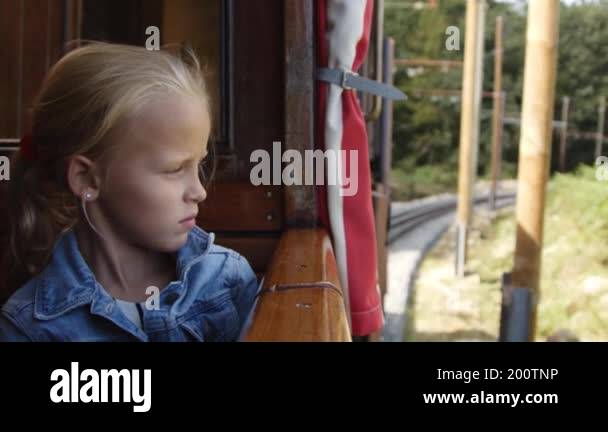 Young girl with blonde hair gazes out the moving train window, admiring the passing scenery and ...
