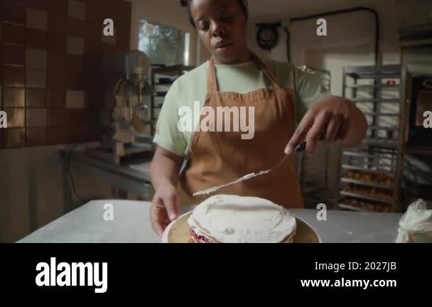 Tilt down shot of skilled African American female pastry chef spreading ...