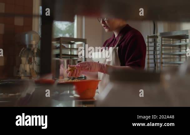 Medium slowmo shot of young female baker in glasses and pink gloves ...